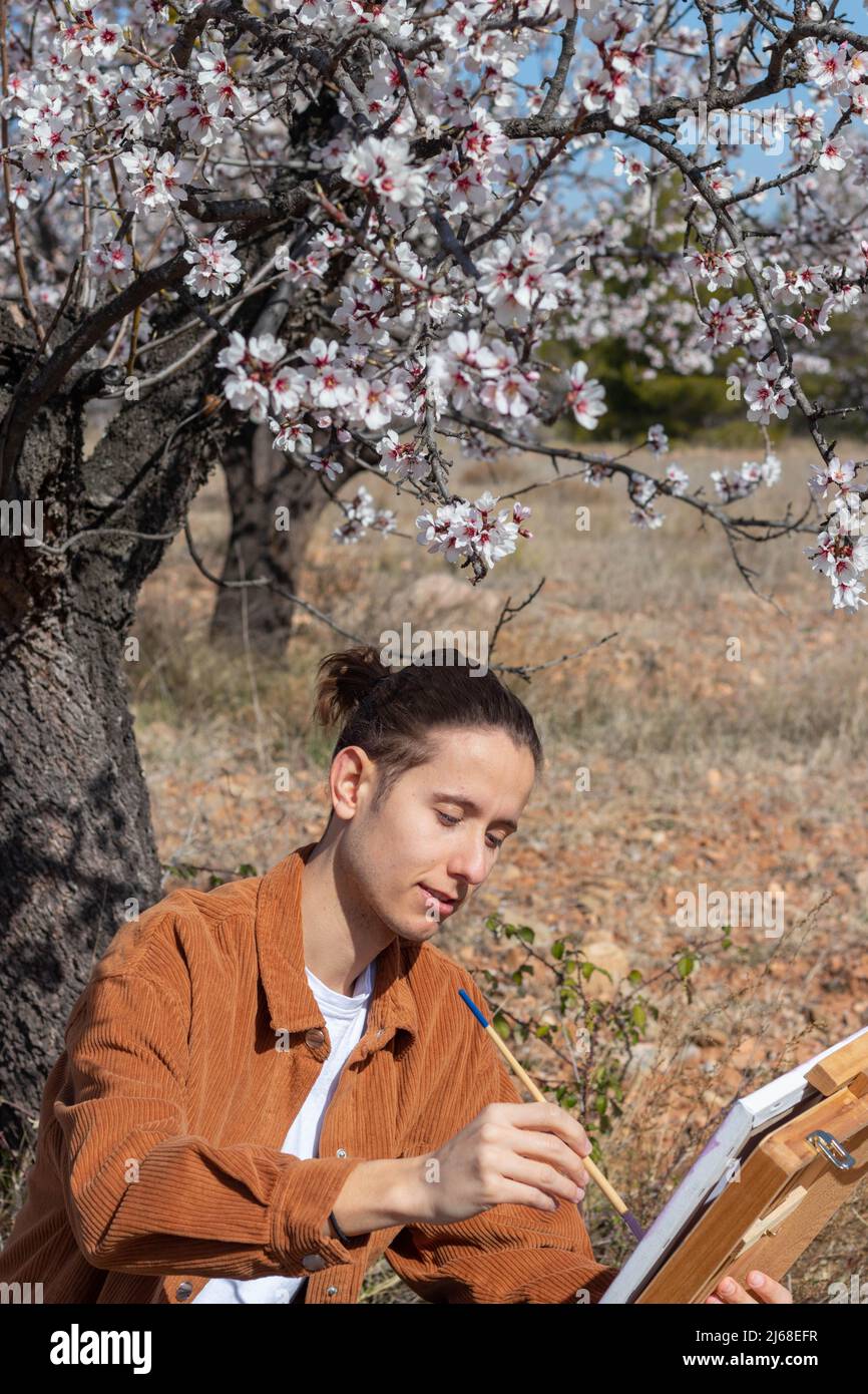 Young man happy and smiling painting a painting under a flowering tree ...