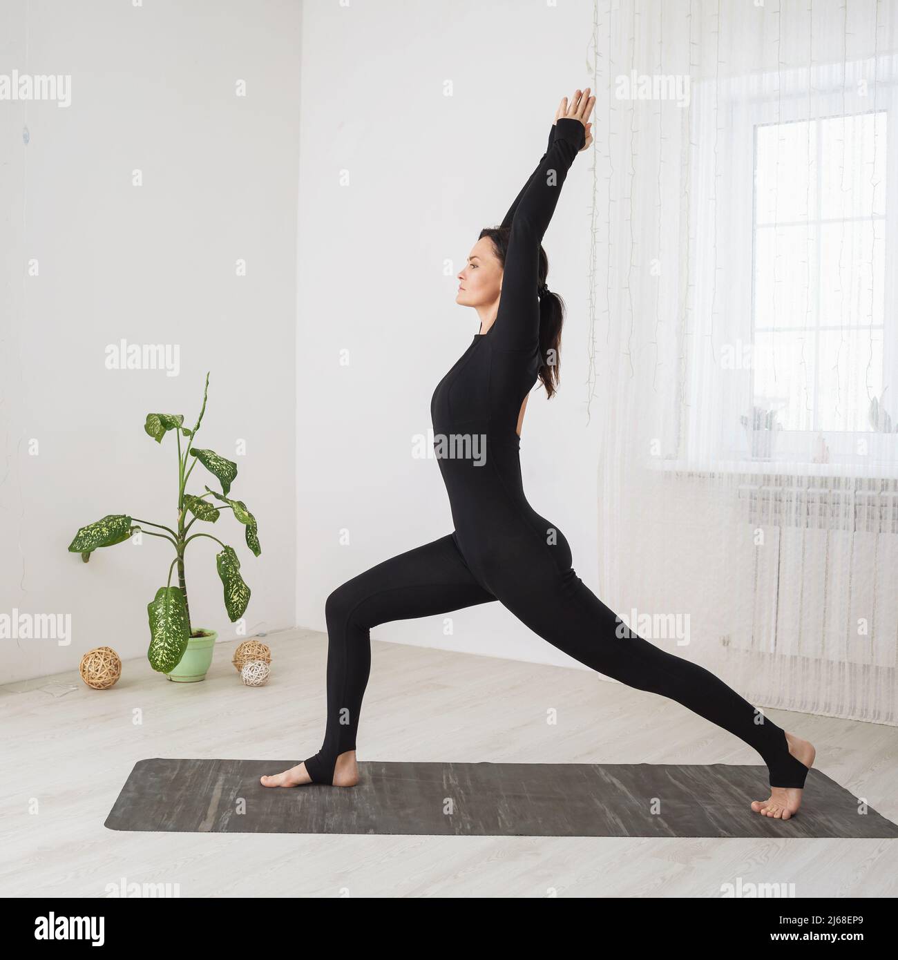 A woman practicing yoga, performs the exercise virabhadrasana, warrior pose, trains while ...