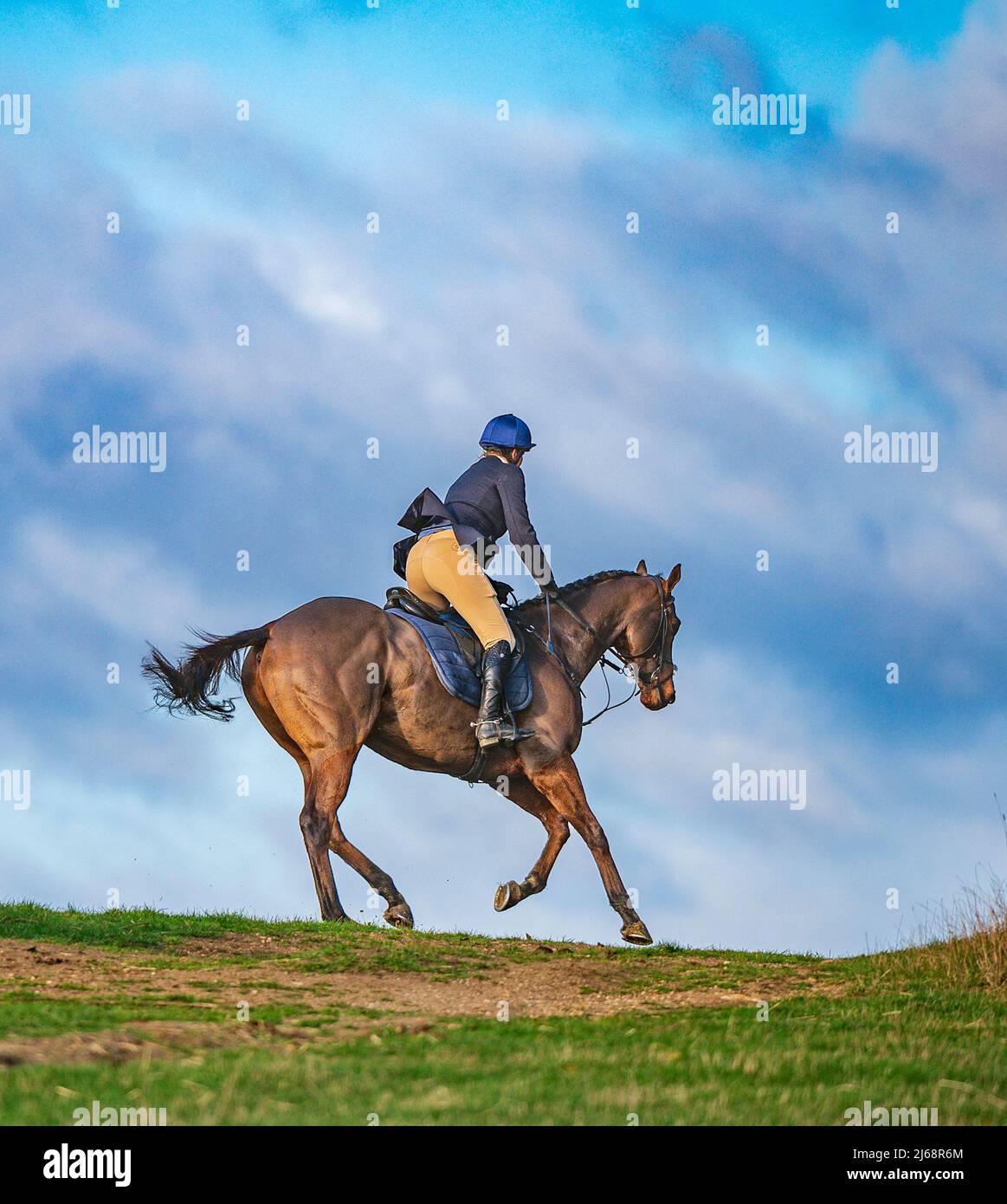 A rider galloping across the skyline on a horse against a stormy sky ...