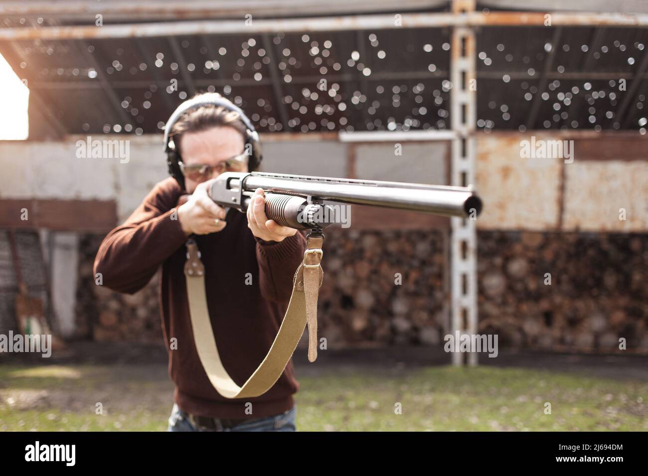 A young man in protective glasses and headphones. A pump-action shotgun ...