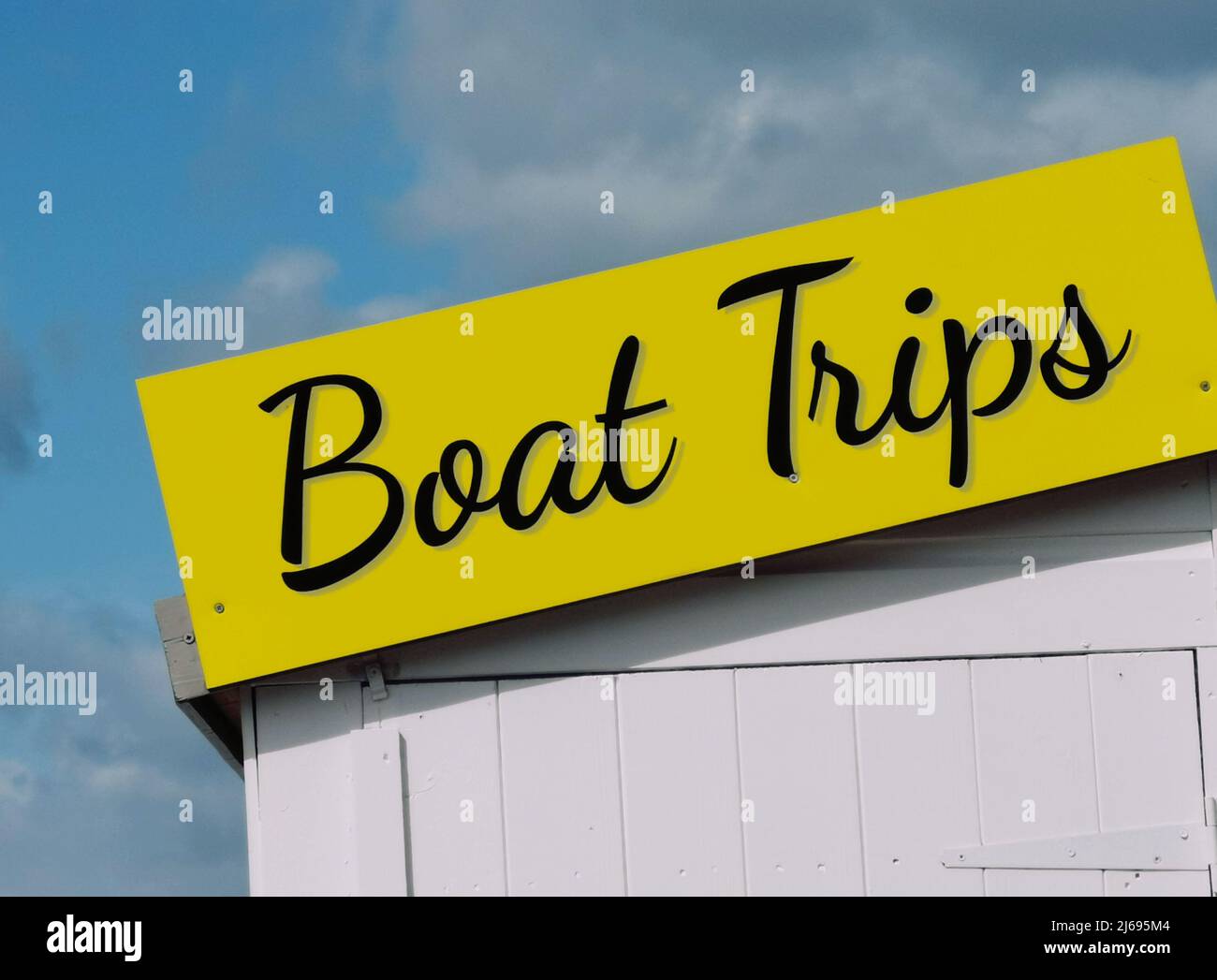 Yellow and black sign indicating Boat Trips attached to white wooden ...