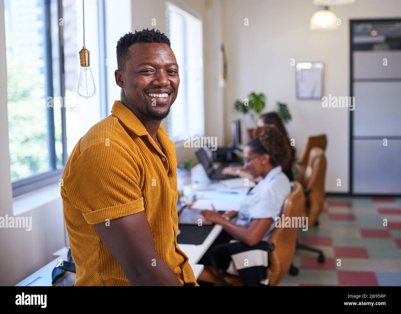 A Black business leader with his team in their creative open-plan ...