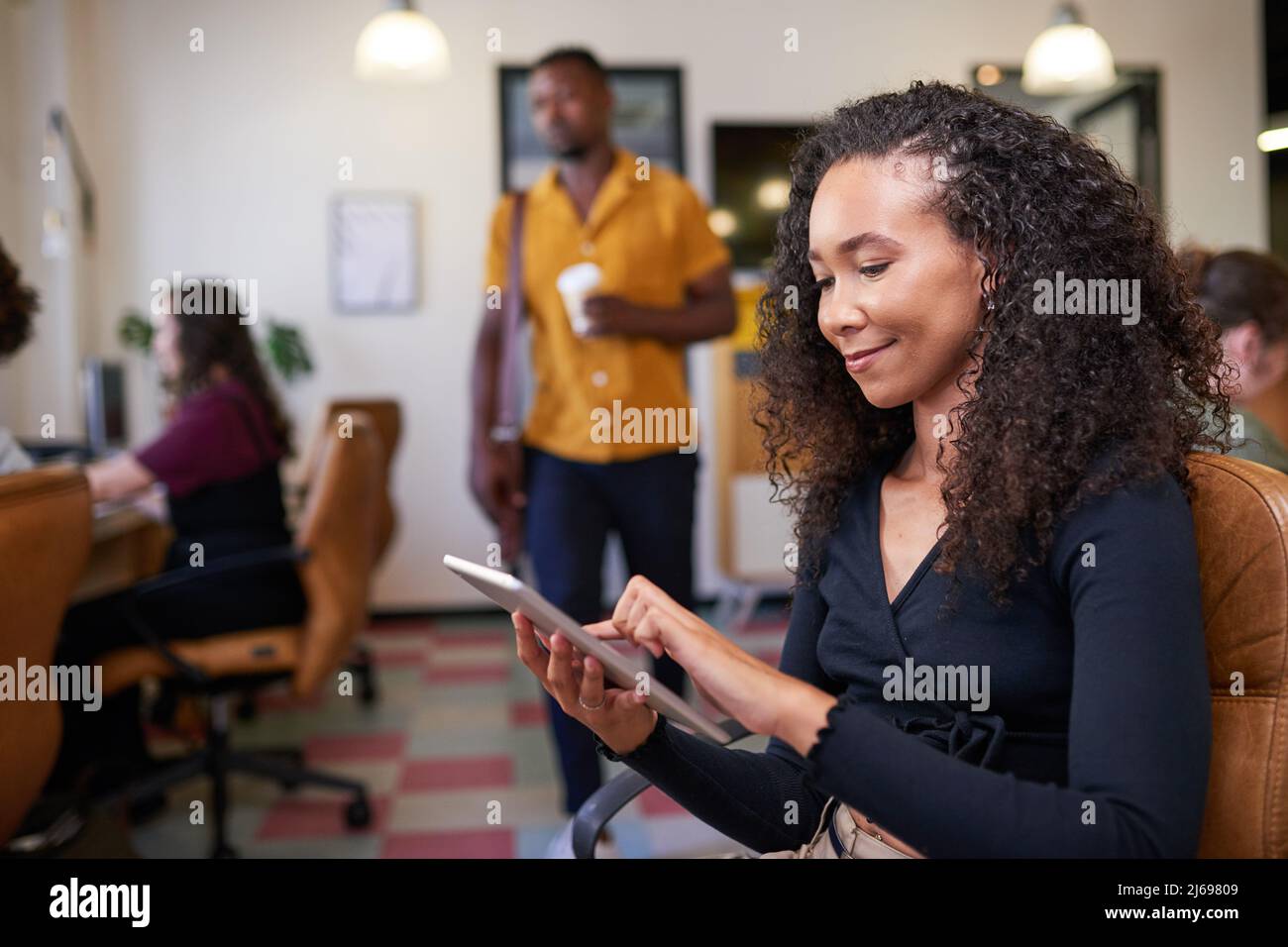 A young multi-ethnic woman scrolls on her tablet in a busy office Stock ...