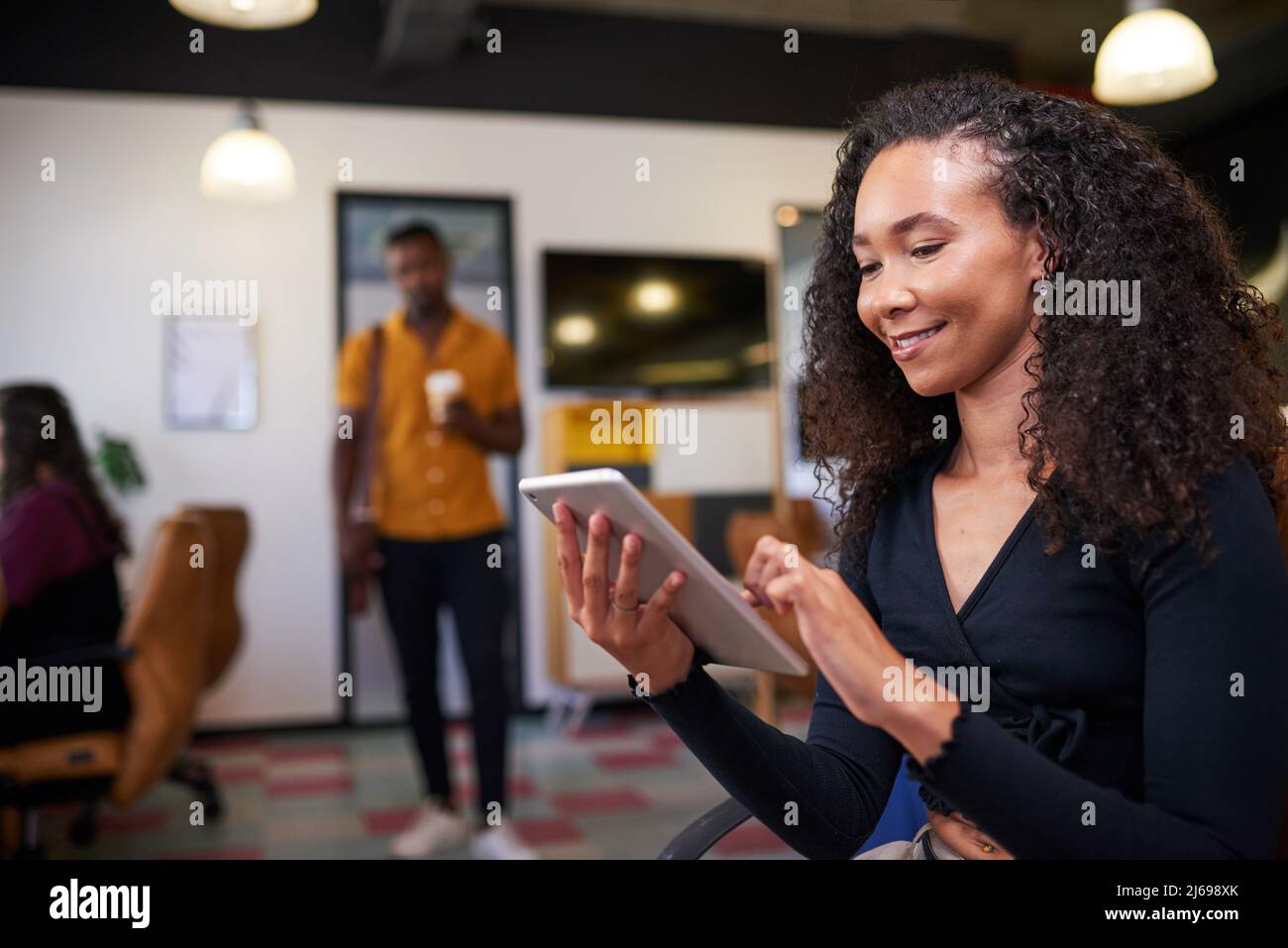 A young multi-ethnic woman scrolls on her tablet while her colleague ...