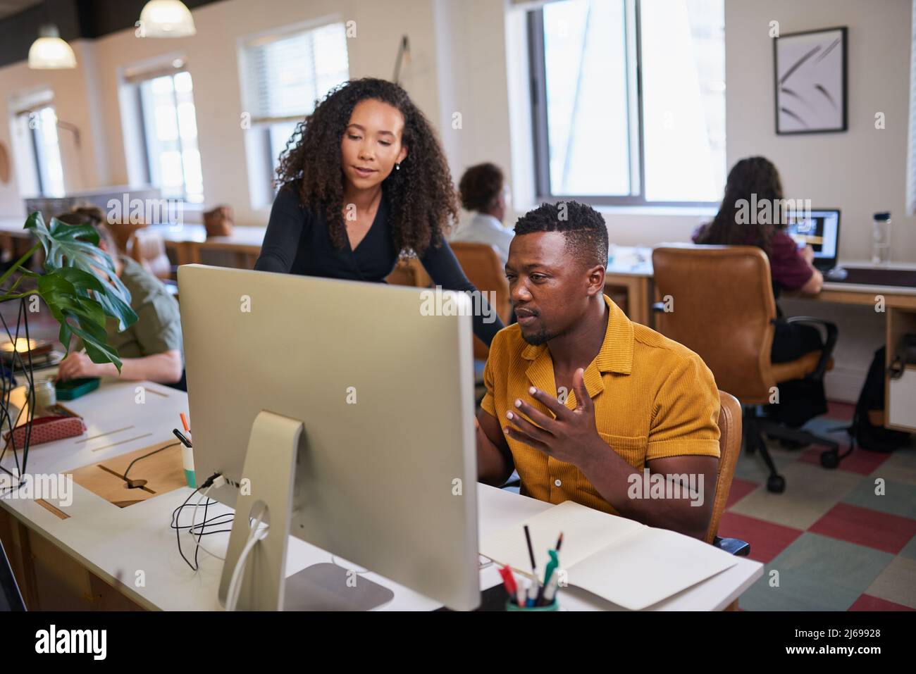 An office scene with two colleagues in discussion while looking at a ...