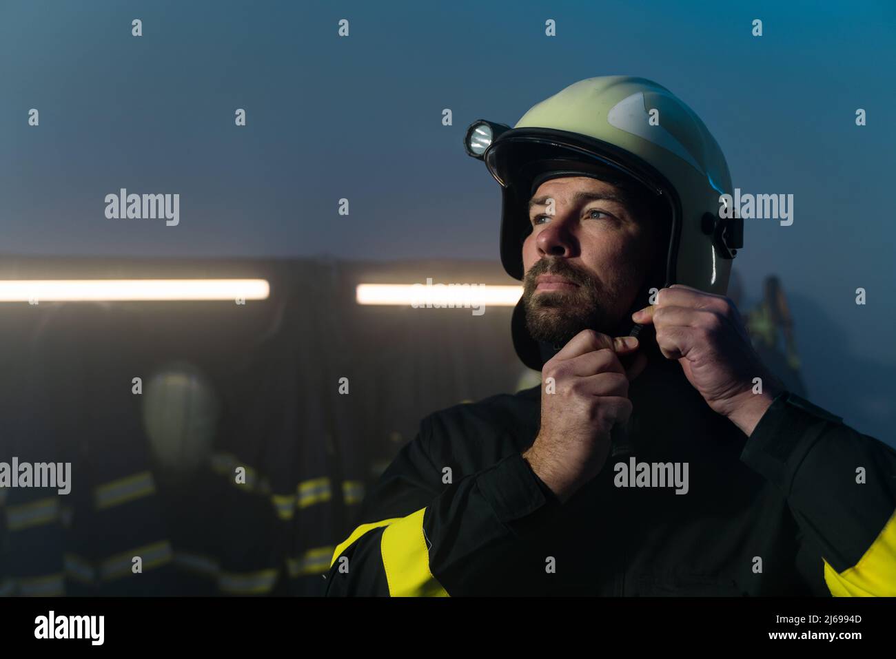 Mature firefighter preparing for action in fire station at night ...