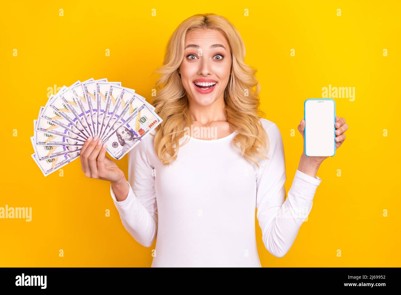 Photo of impressed young blond lady hold telephone money wear white ...
