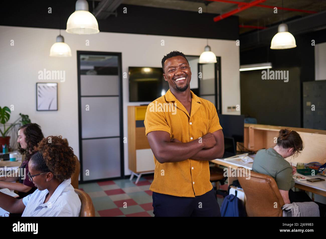 A Black business owner stands with his arms crossed while creative team ...