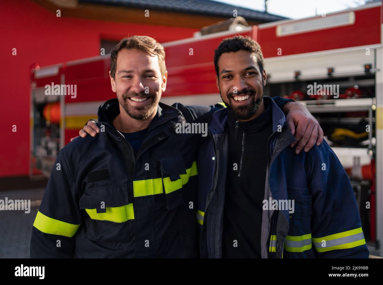 Happy firefighters crew with fire station and truck in background ...