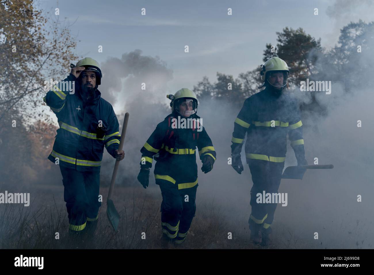 Firefighters men at action, running through smoke with shovels to stop ...