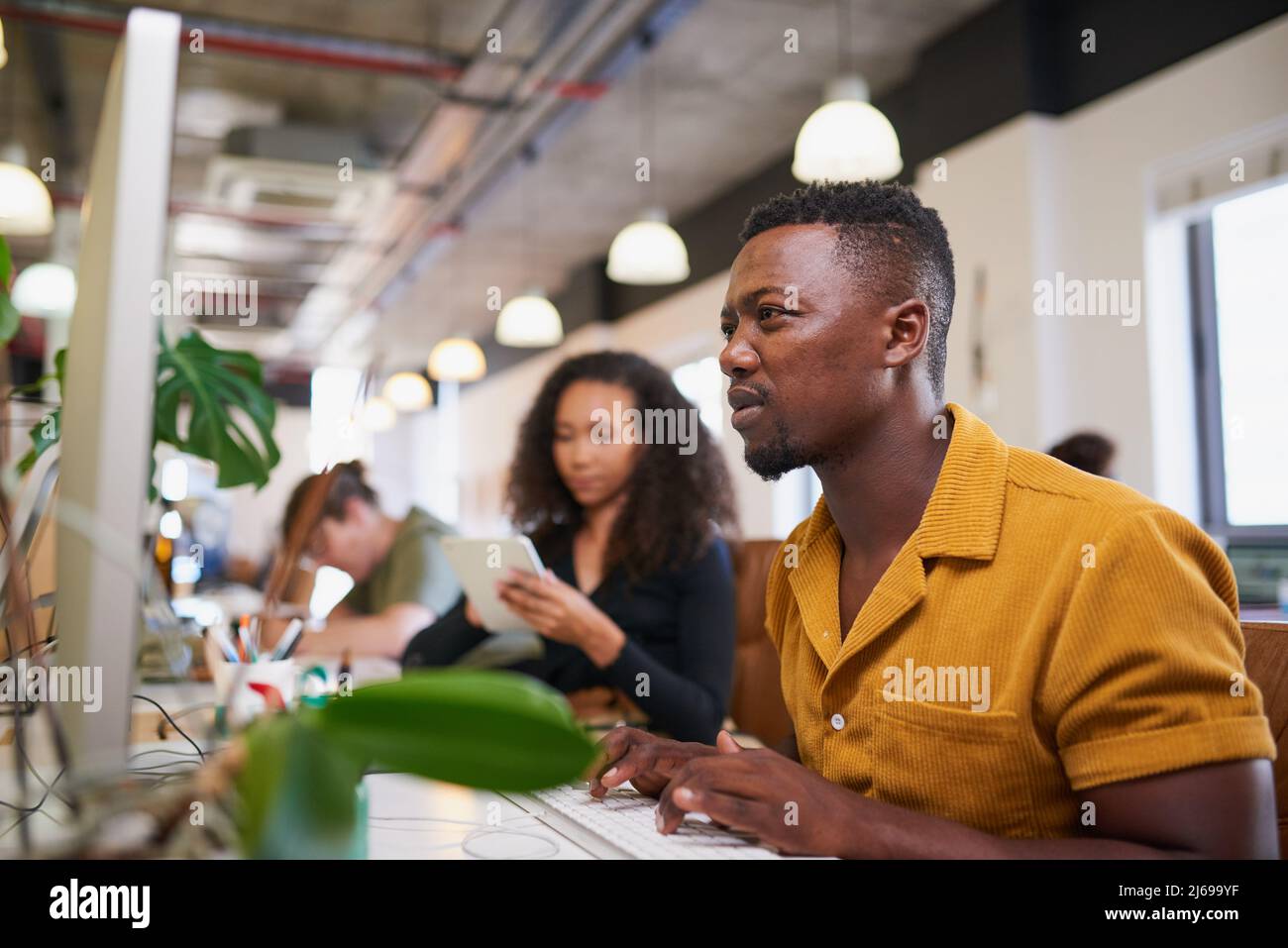 A Black man squints at his computer screen in a busy creative office ...