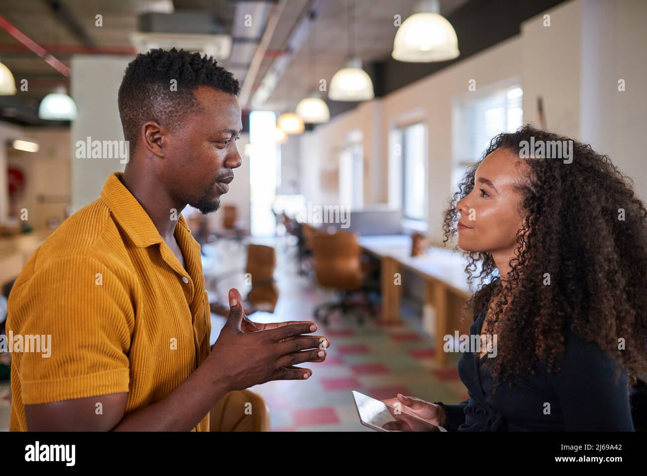 Two colleagues have a discussion in an open plan creative office Stock ...