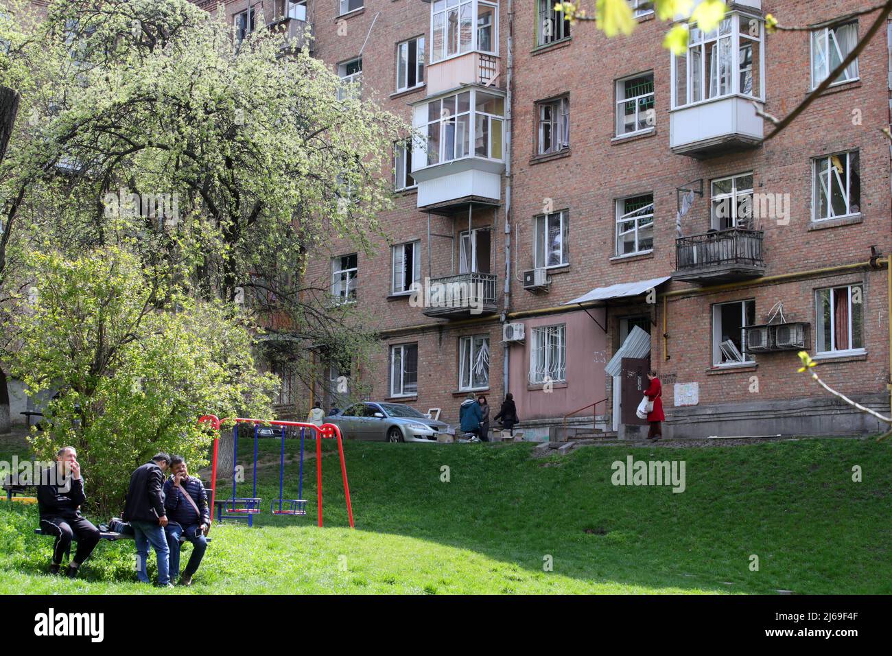 KYIV, UKRAINE - APRIL 29, 2022 - Men sit on a bench outside a damaged ...