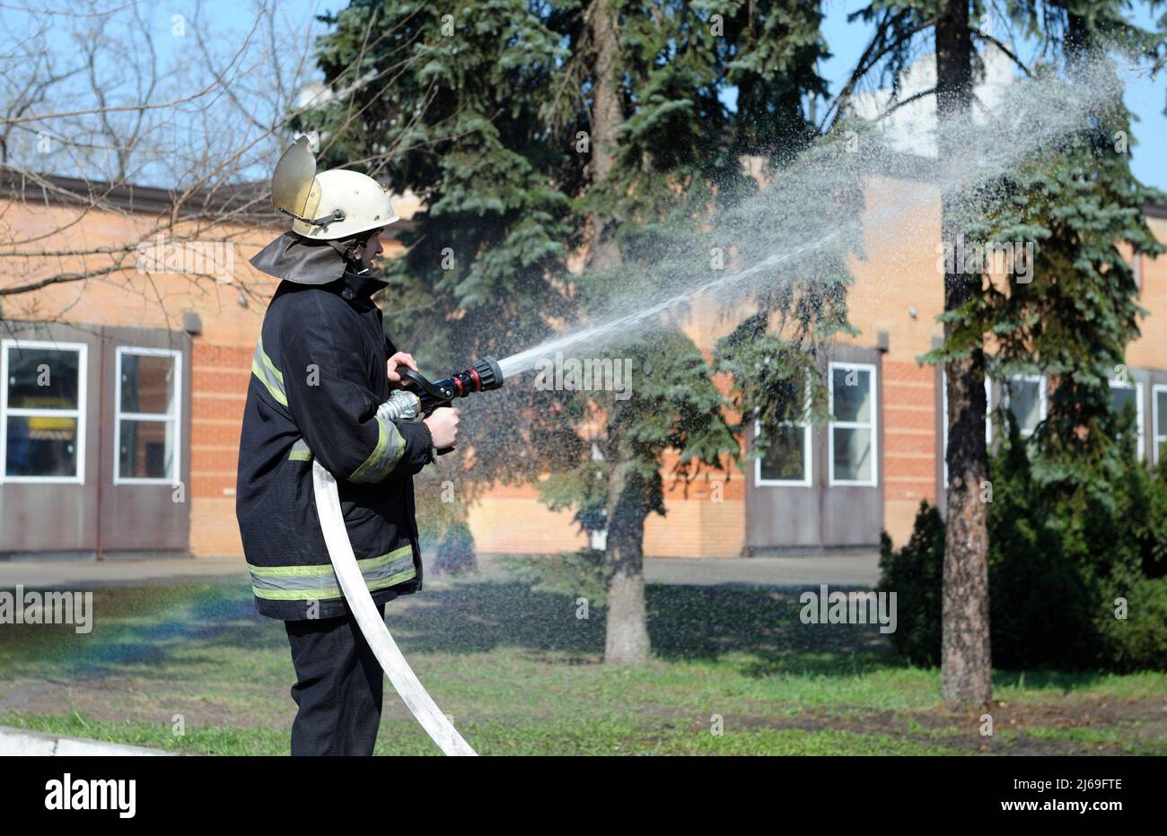 Fireman in protective costume watering plant territory with syringe ...