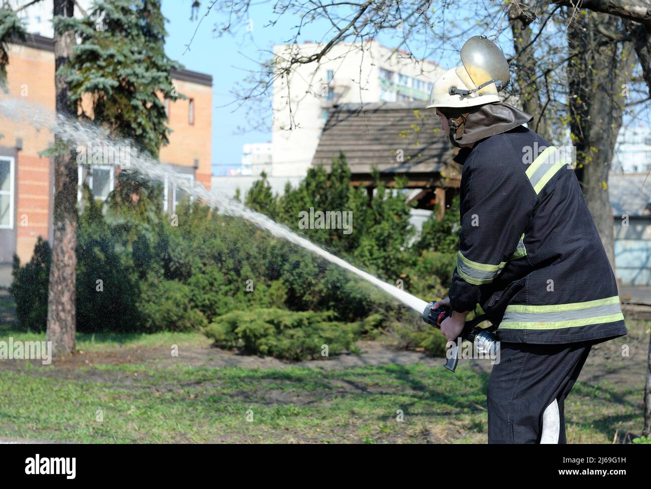 Fireman in protective costume watering plant territory with syringe ...