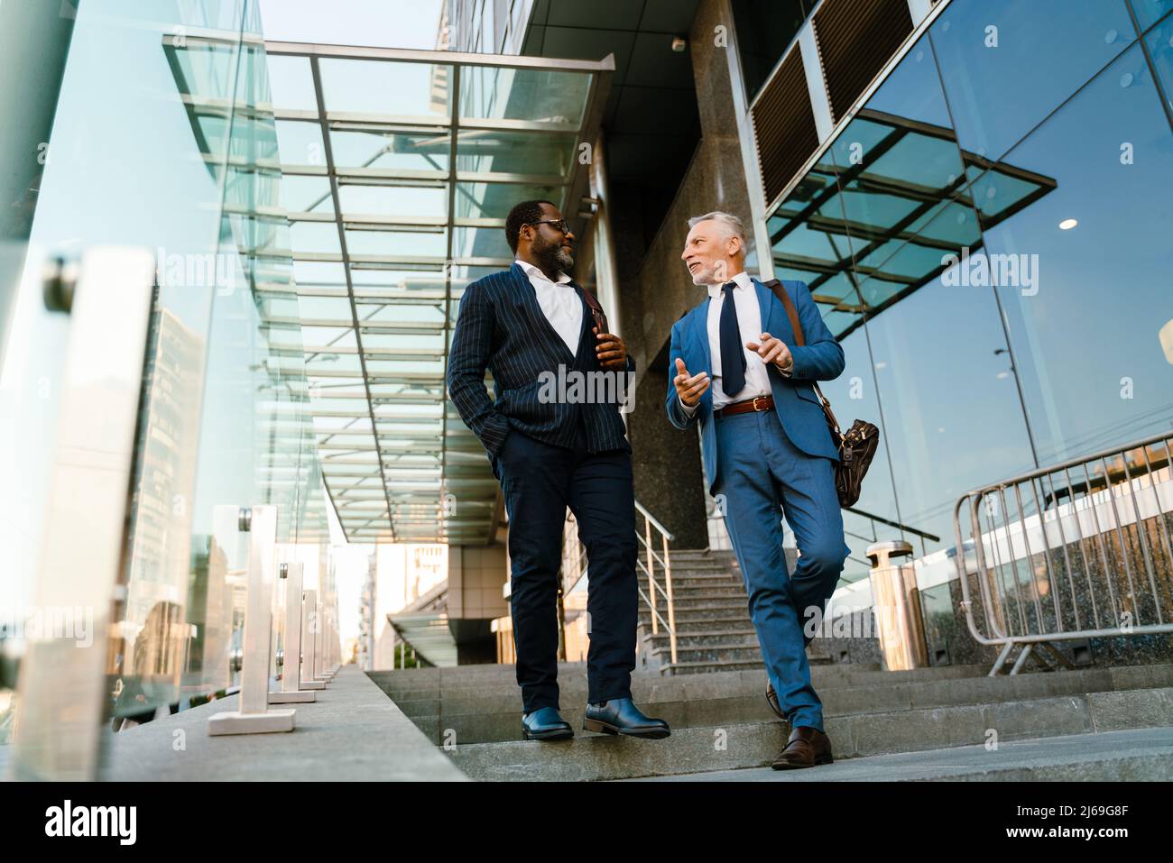 Multiracial men dressed in suits talking and gesturing while going down ...