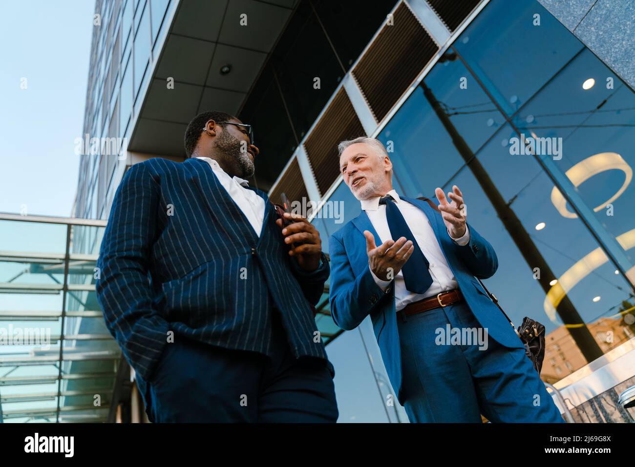 Multiracial men dressed in suits talking and gesturing while going down ...