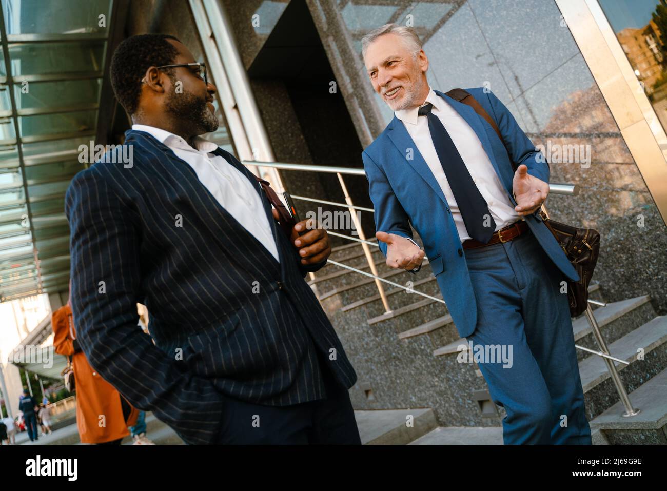 Multiracial men dressed in suits talking and gesturing while going down ...