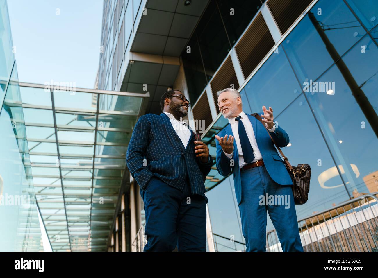 Multiracial men dressed in suits talking and gesturing while going down ...
