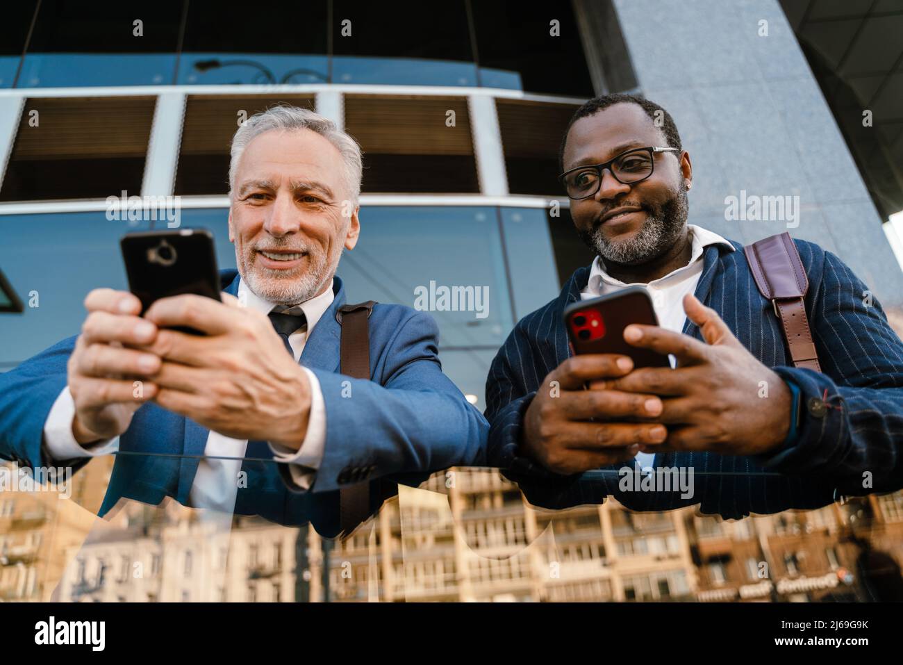 Multiracial men talking and using cellphones while standing by building ...