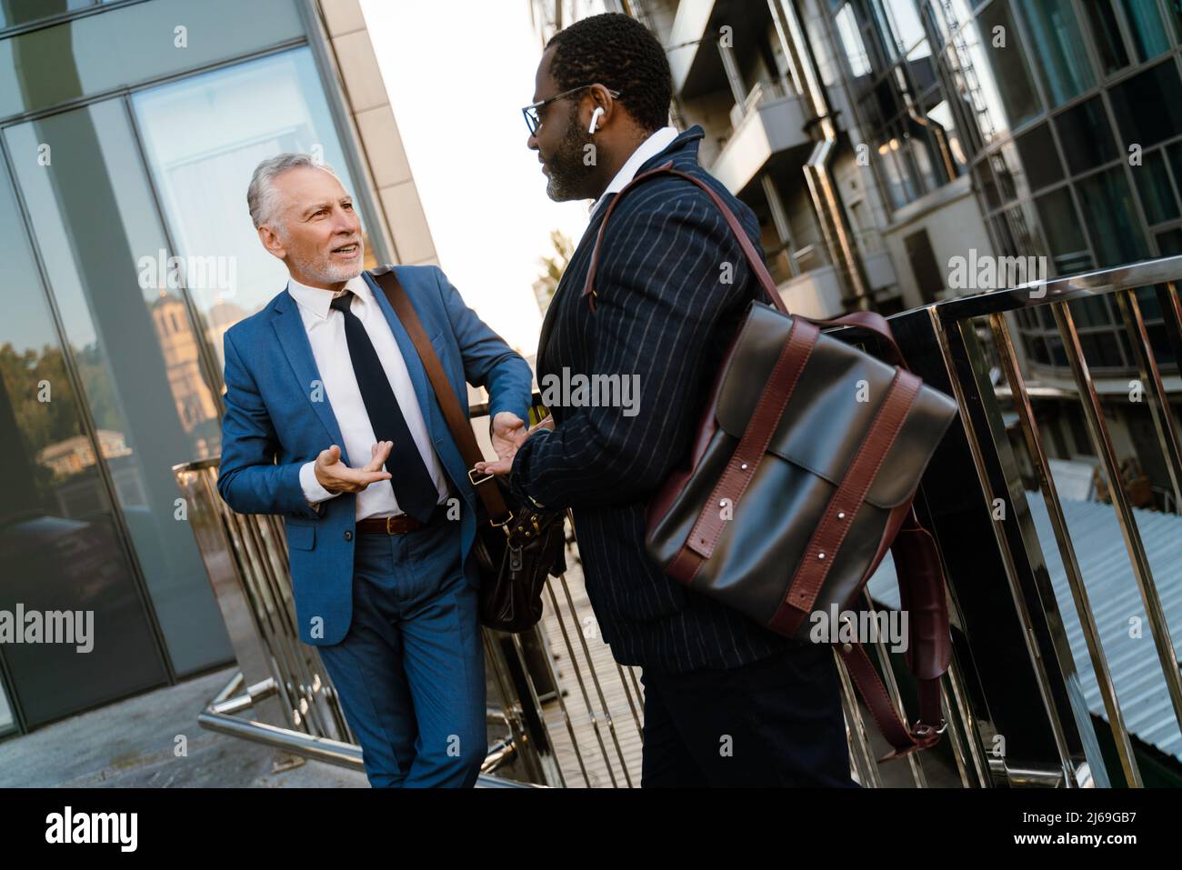 Multiracial men talking and gesturing while standing by building ...