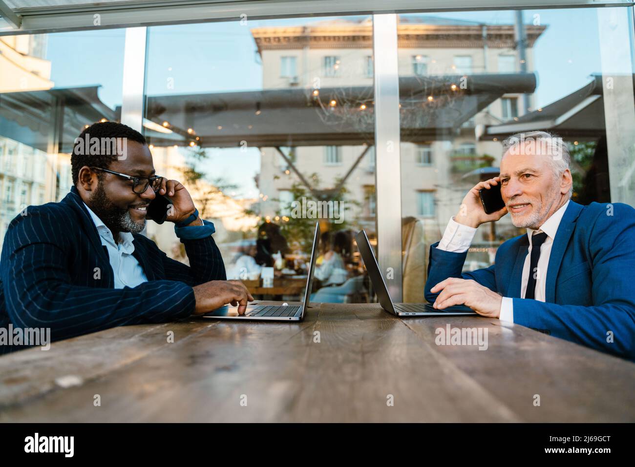 Multiracial men talking on cellphones while working with laptops in ...