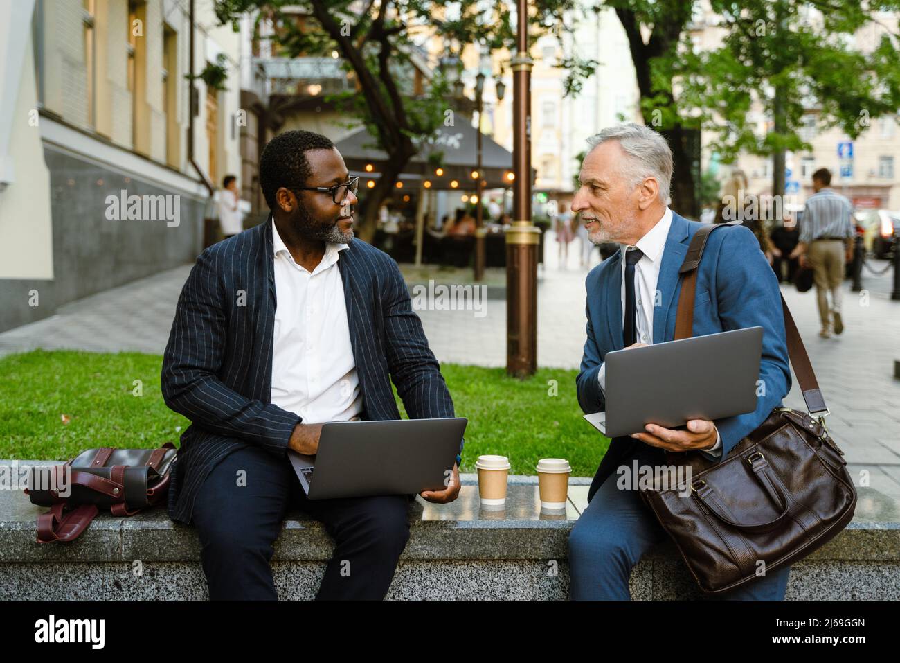 Multiracial men talking while working with laptops and drinking coffee ...