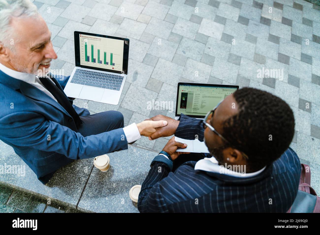 Multiracial men talking and handshaking while working with laptops ...