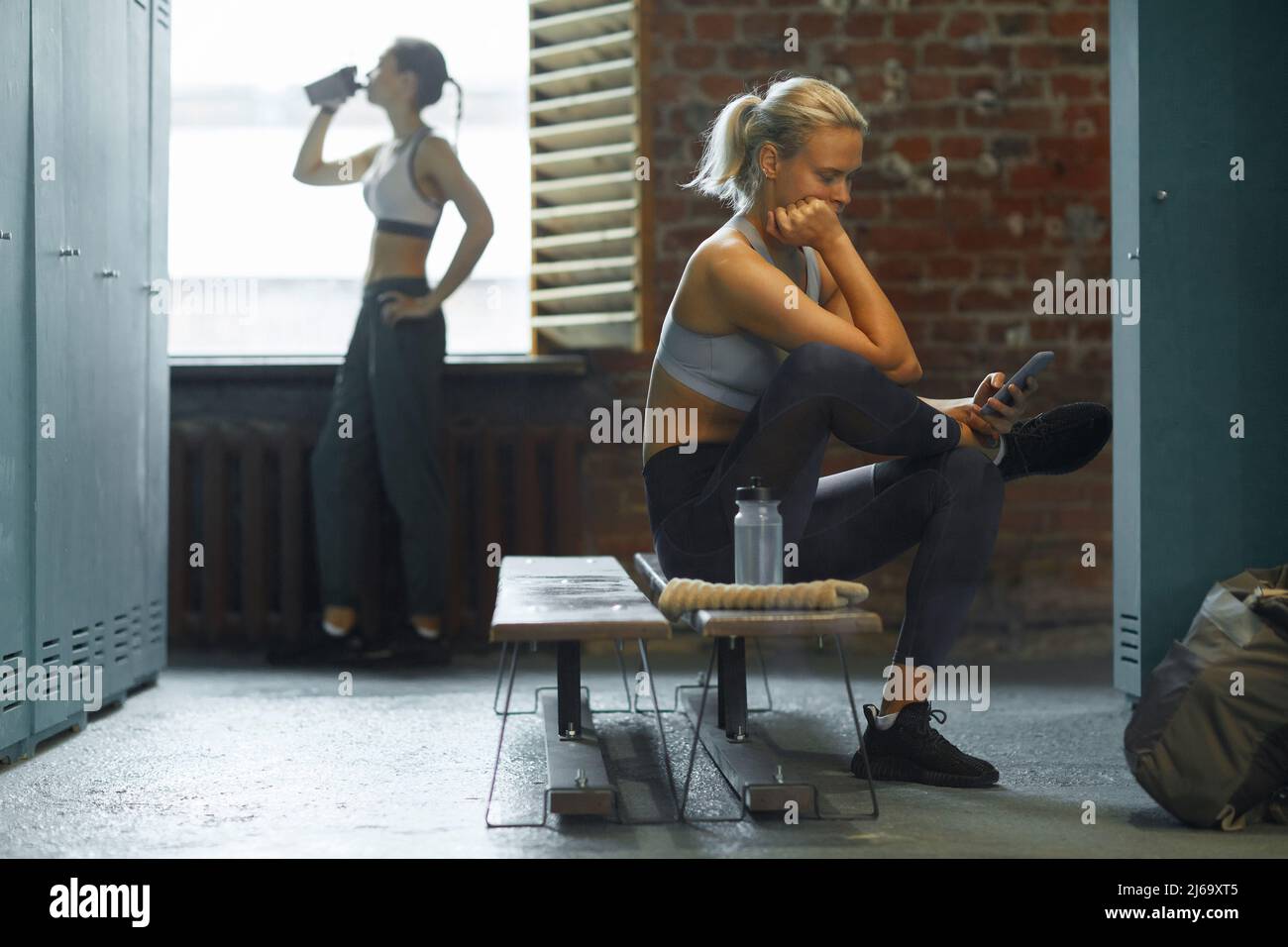 Two relaxed young women spending break time in gym dressing room ...