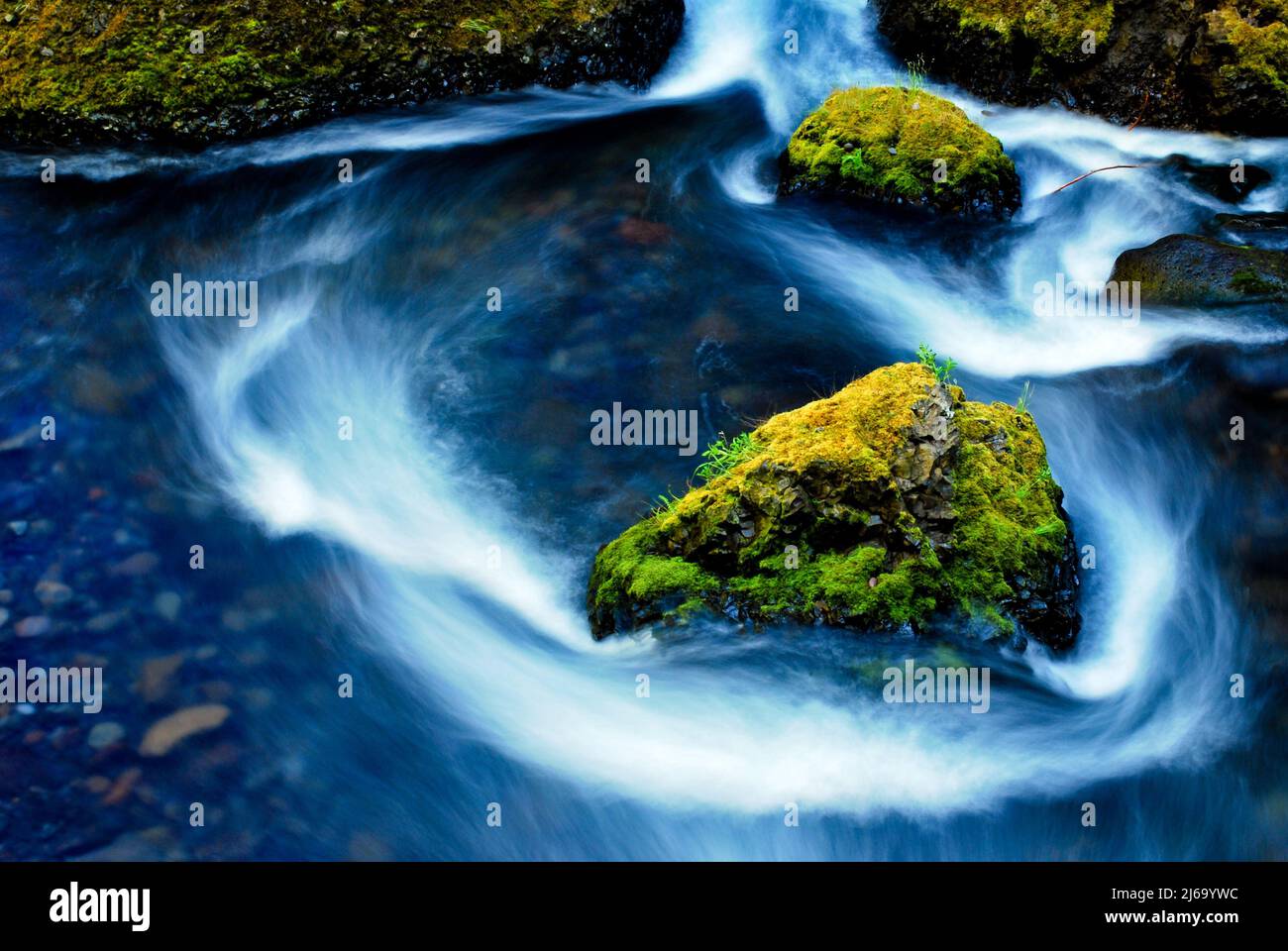 Blue river water rushing by green moss covered rocks Stock Photo - Alamy