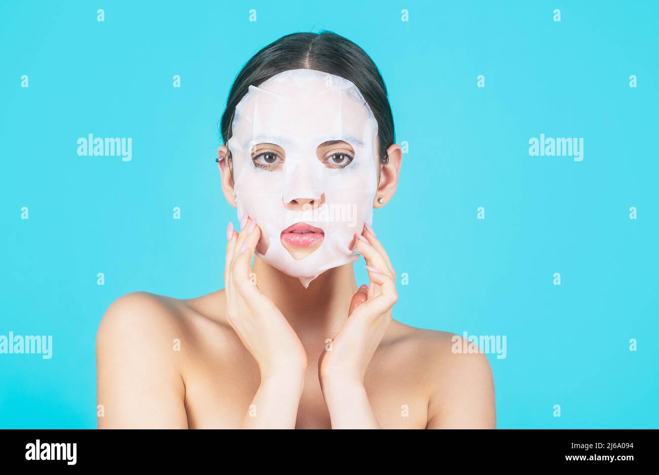 Woman applying sheet mask on her face, on blue background. Beautiful ...