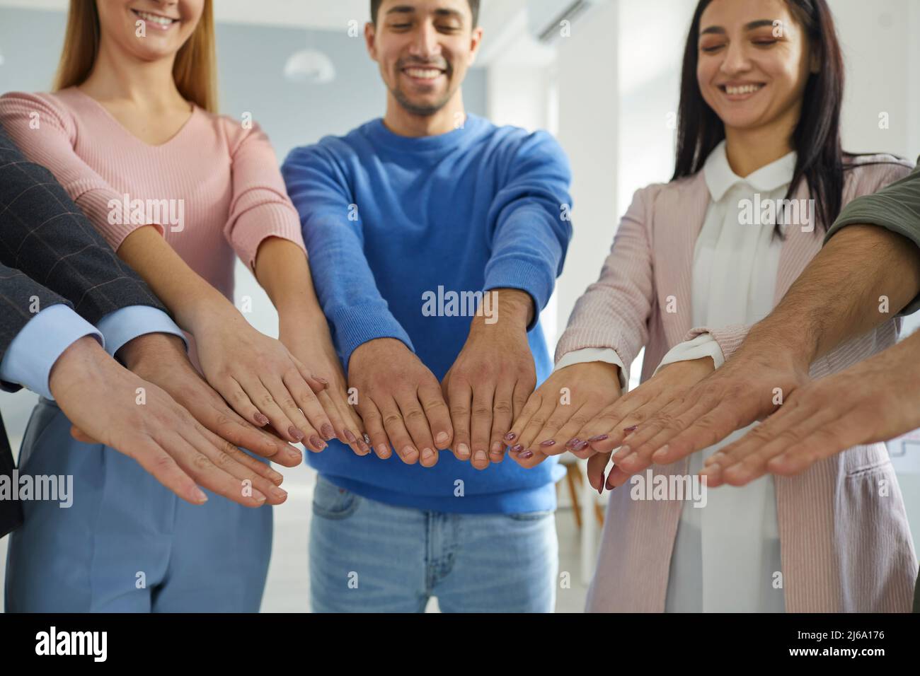 Team of happy business people standing together, joining their hands and smiling Stock Photo - Alamy