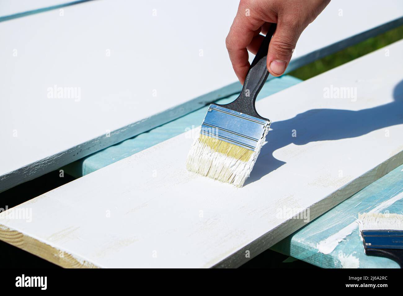 Male builder paints white boards for construction. Male hand holds ...