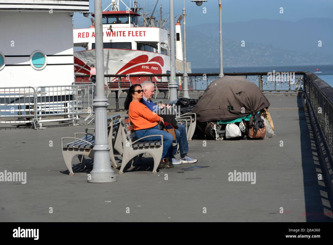 Tourists sit on a pier near the makeshift shelter of a homeless man in ...