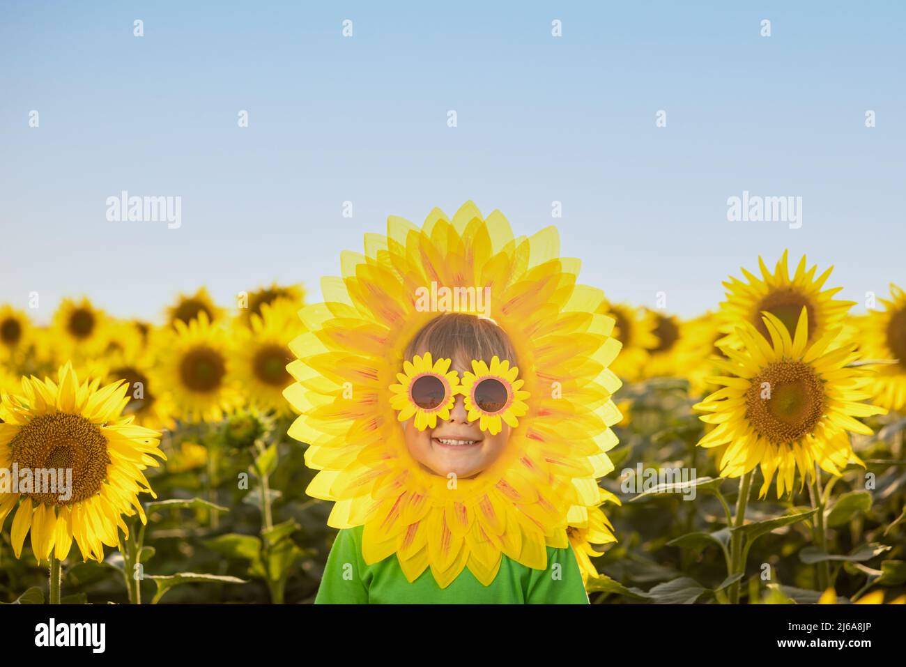 Happy child having fun in spring field of sunflowers. Outdoor portrait ...