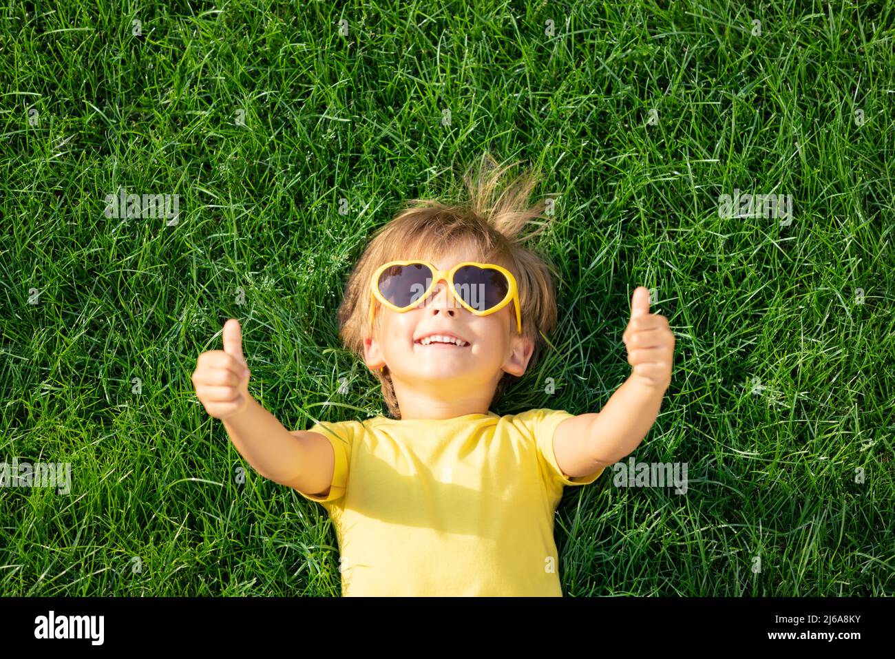 Happy child playing outdoor in spring park. Kid lying on green grass ...