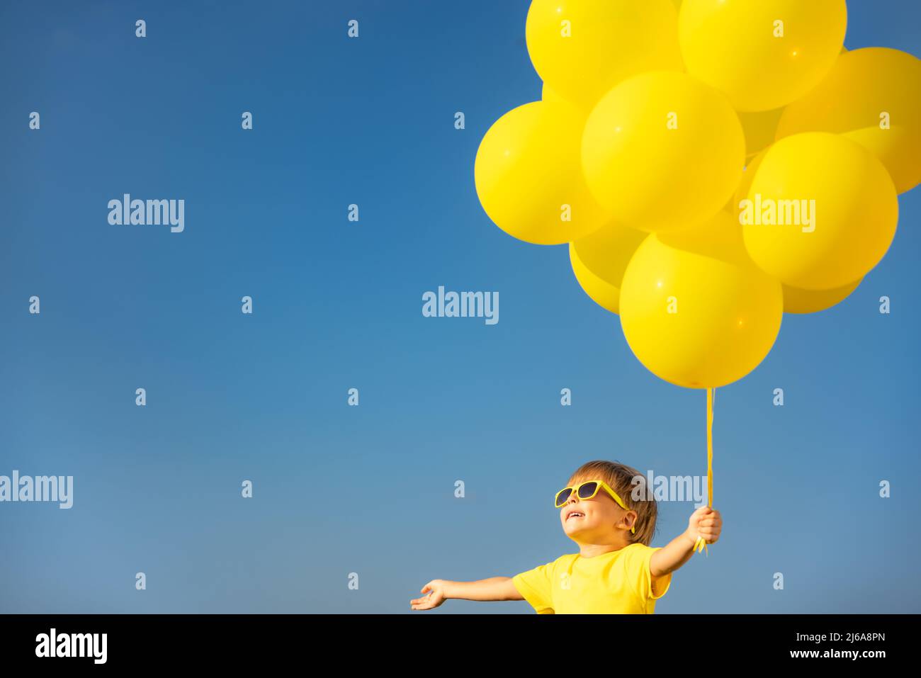 Happy child playing with yellow balloons outdoor. Kid having fun ...