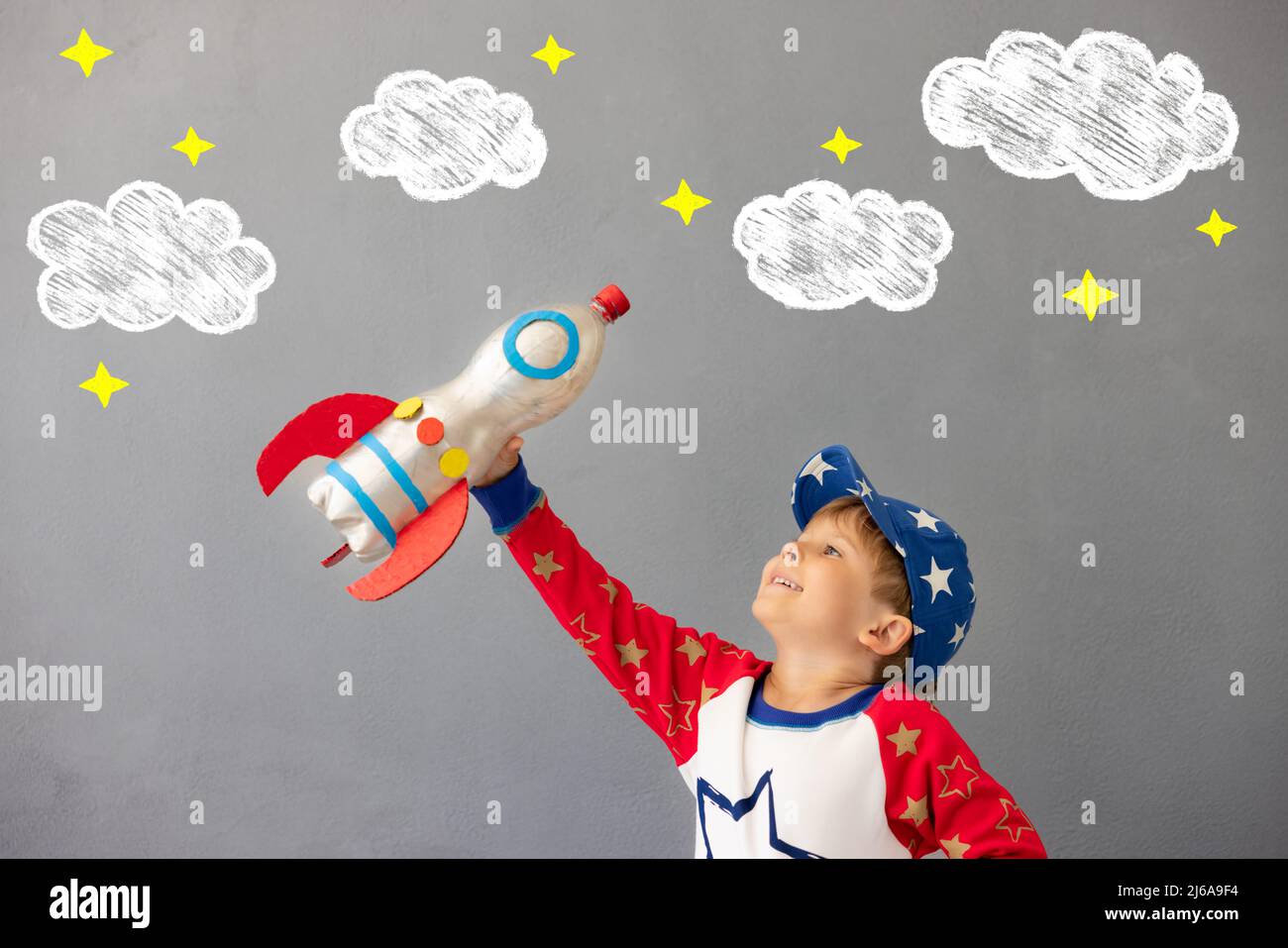 Happy child playing with toy rocket against concrete wall background ...