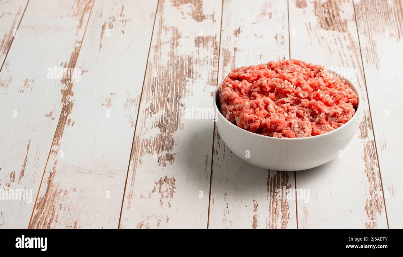 Plate with fresh ground beef on a brown wooden background, space for ...