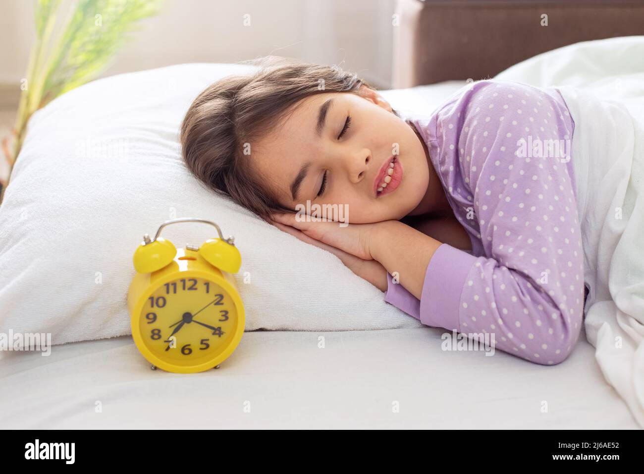 A sleeping brunette girl in purple polka dot pajamas lie on a white ...
