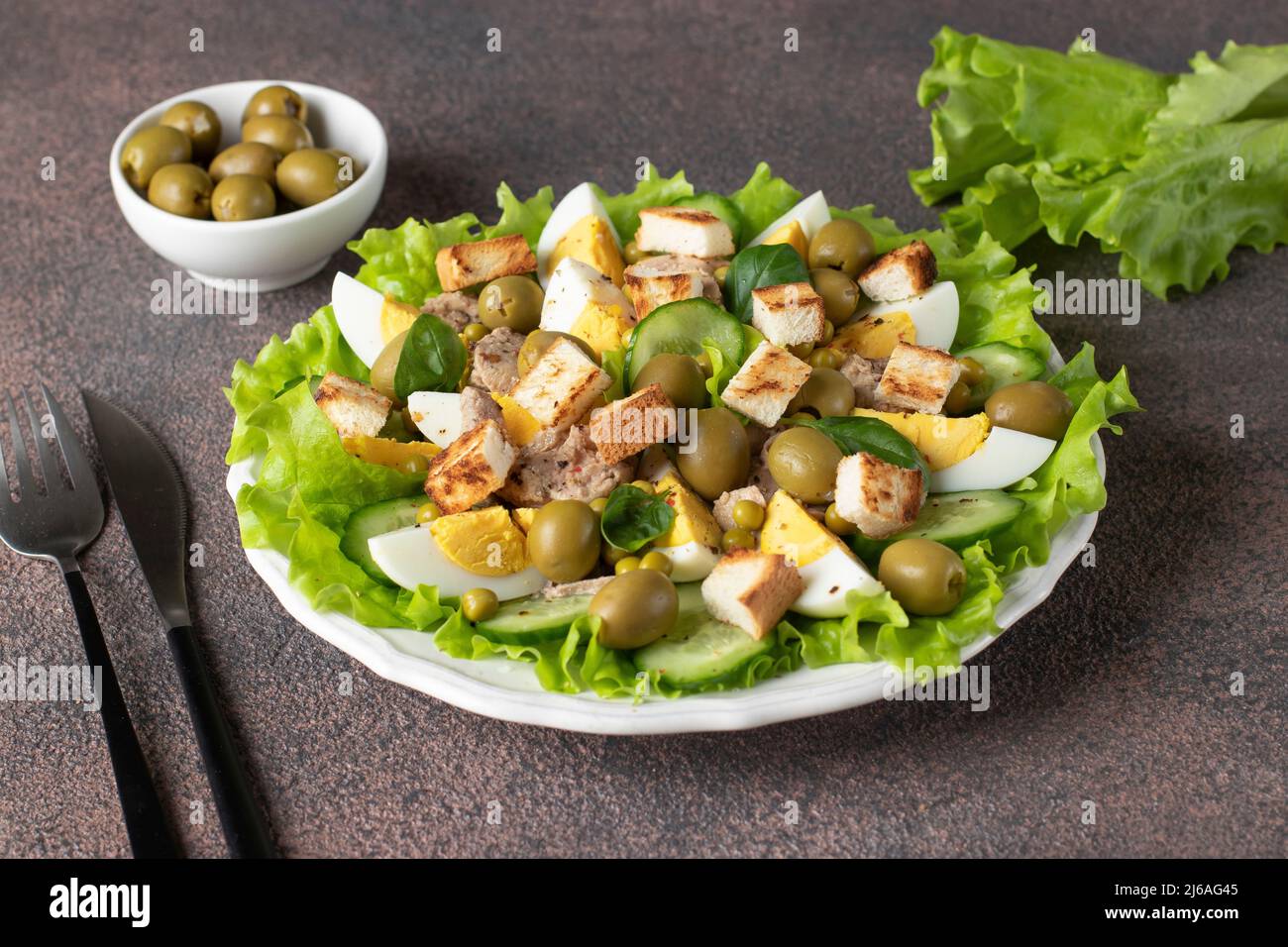Salad with cod liver, egg, cucumber, olives and croutons, served on ...