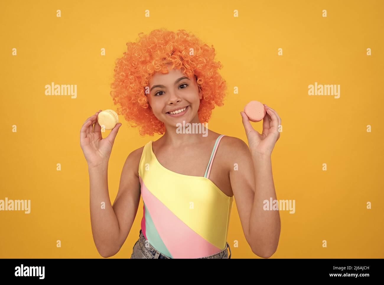 happy teen girl in swimsuit wearing wig hold french macaron on yellow ...