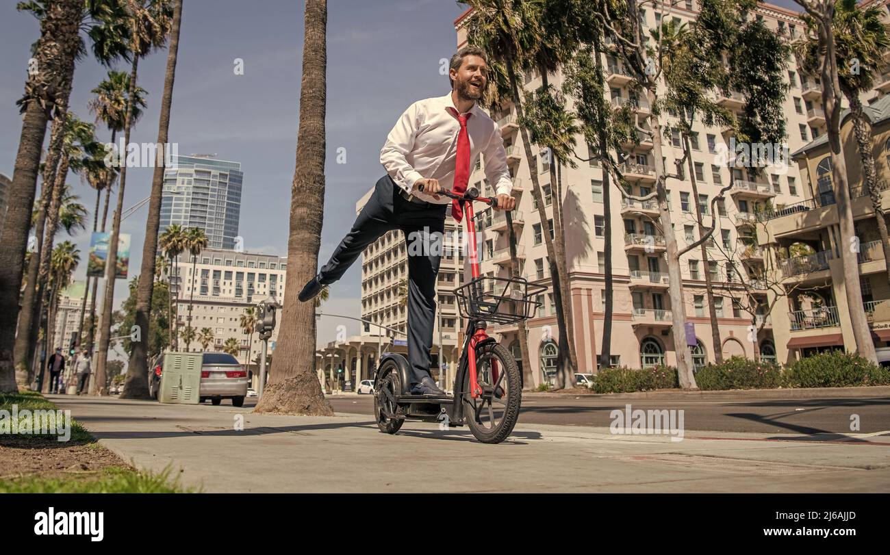 Happy director in formalwear ride stand-up e-scooter along sidewalk ...