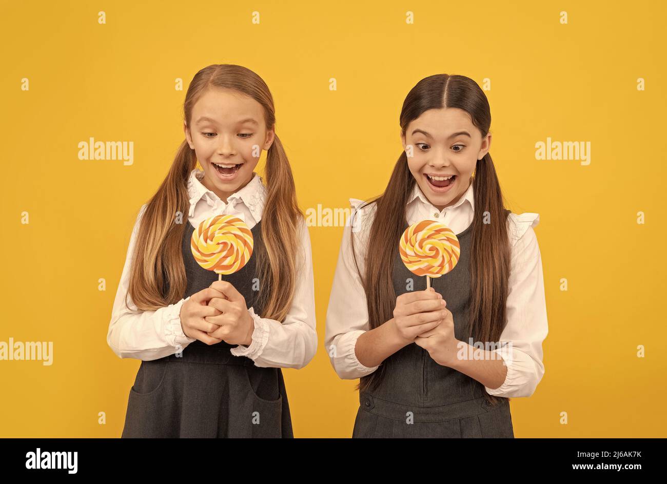 Super yummy. Candy girls yellow background. Suprised kids hold candy ...