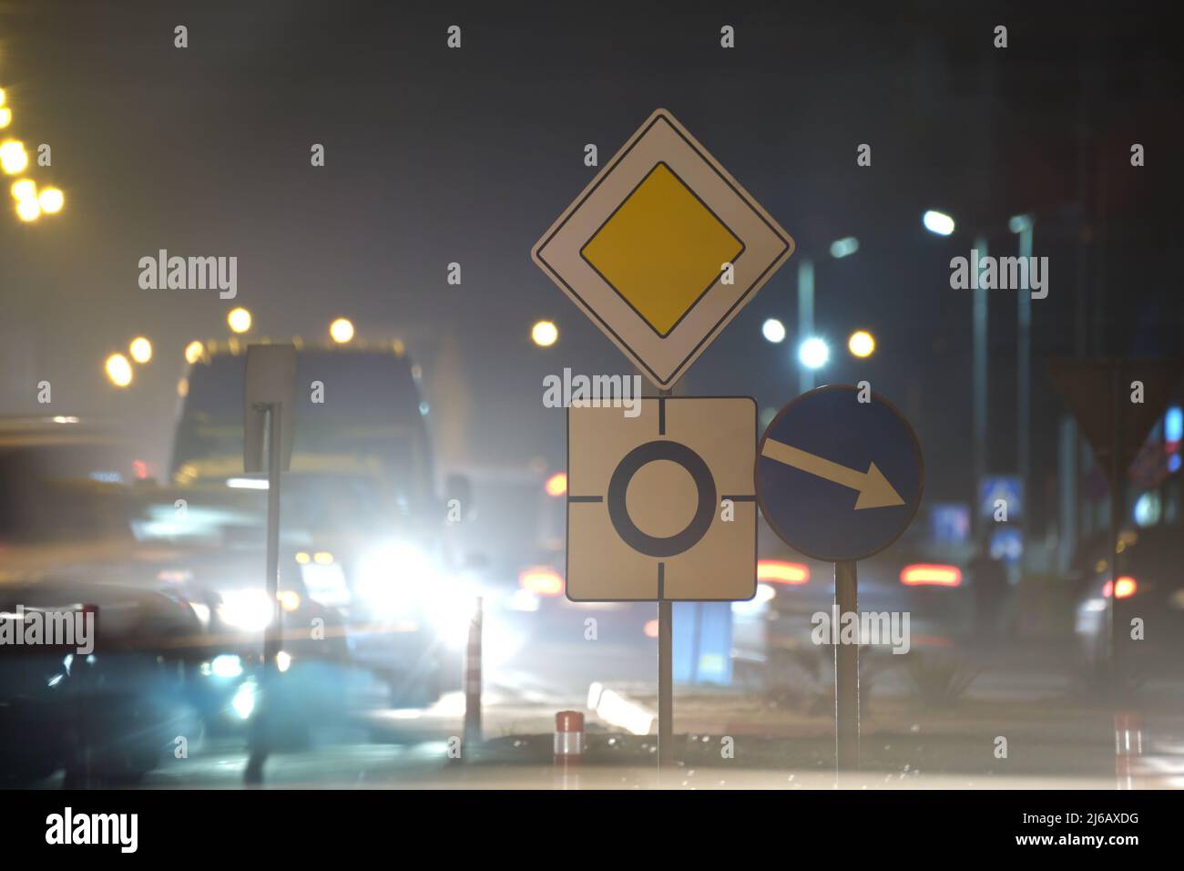 Roundabout road signs with blurred cars on city street traffic at night ...