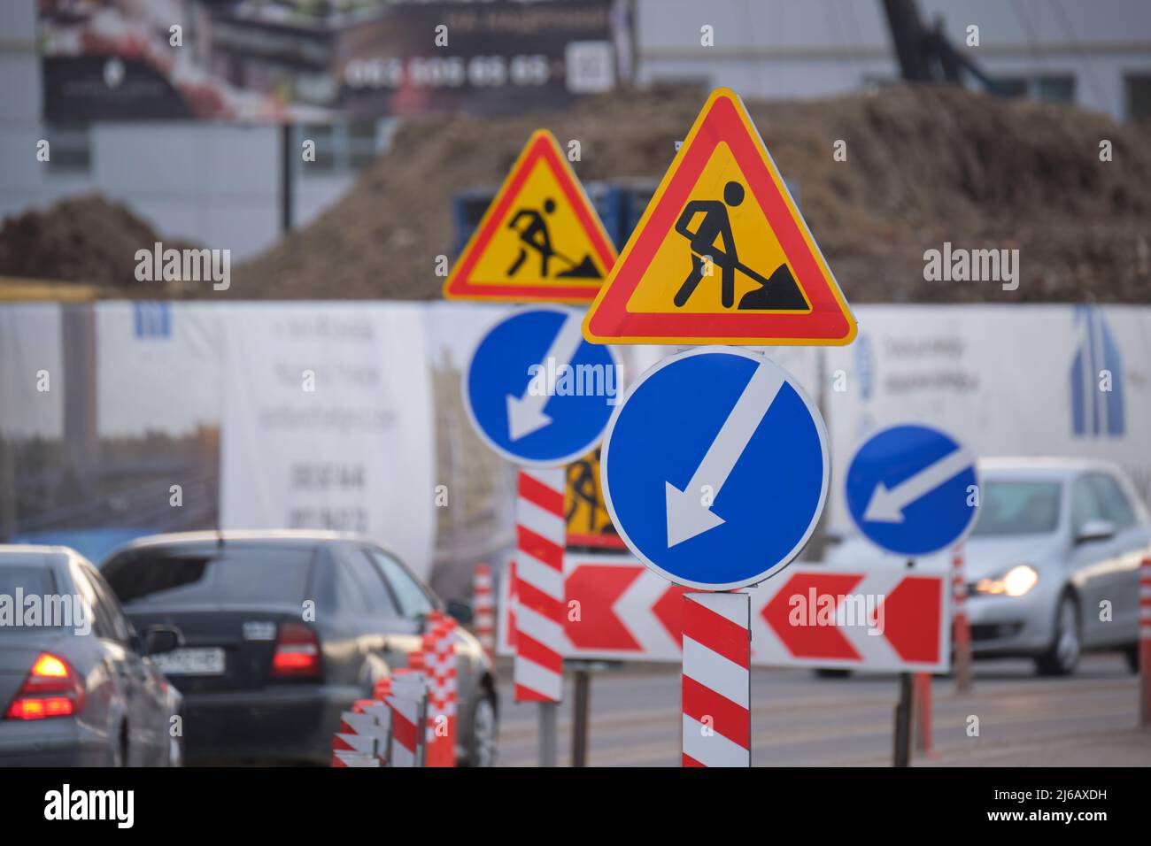 Roadworks warning traffic signs of construction work on city street and slowly moving cars Stock ...