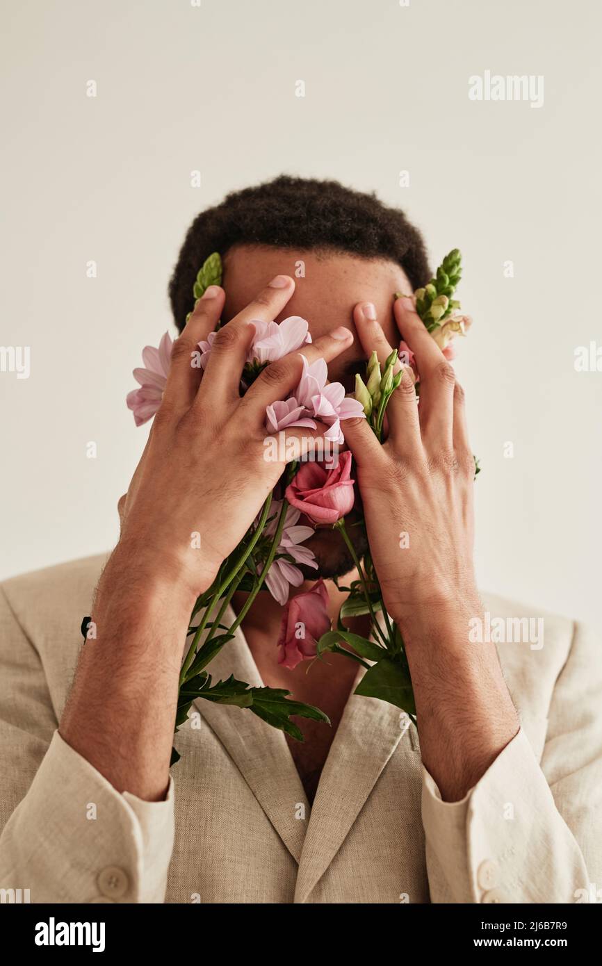 Portrait of young man covering his face with hands with flowers against ...