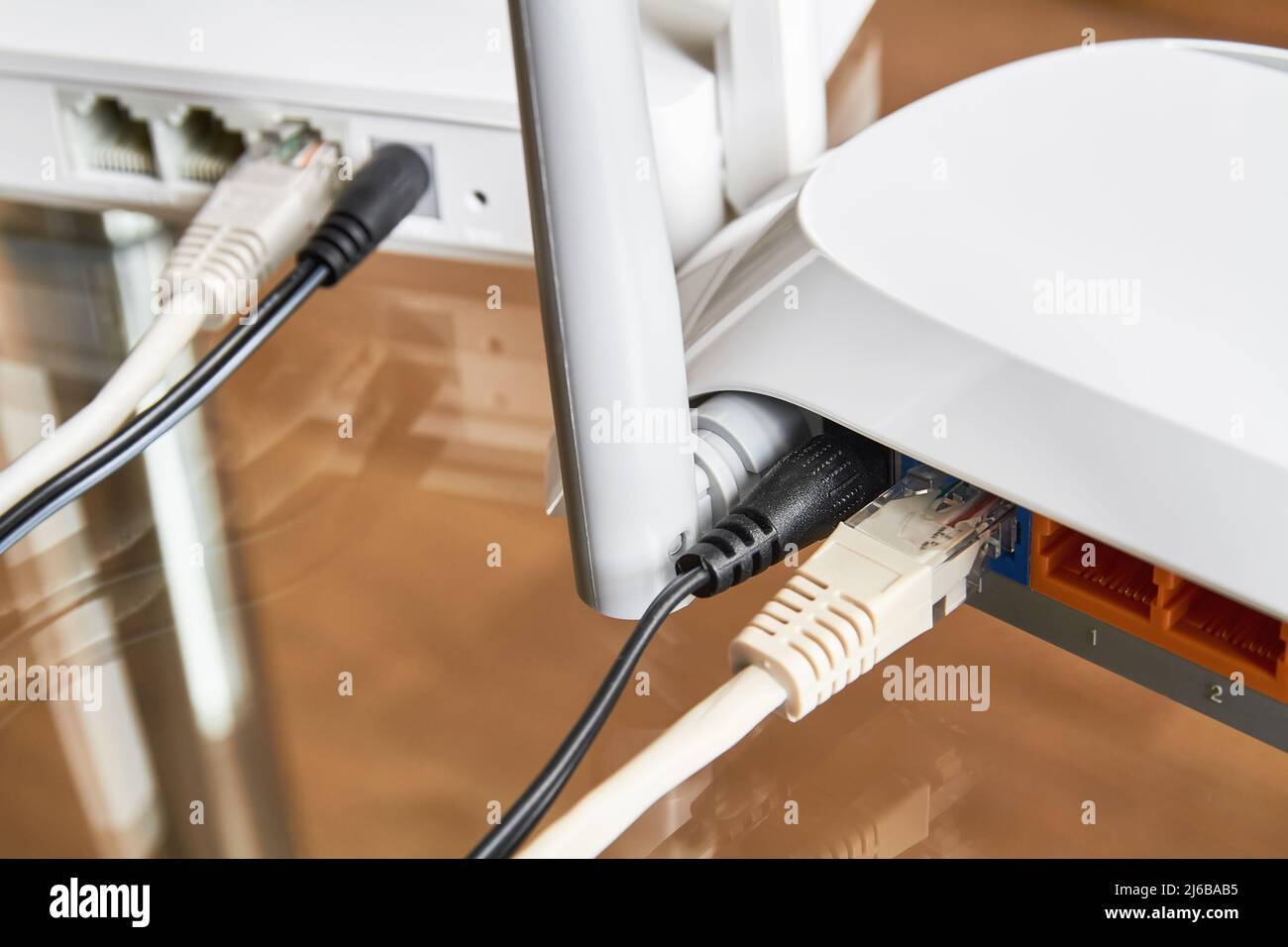 Two white wireless routers on a glass table connected by cables to the ...