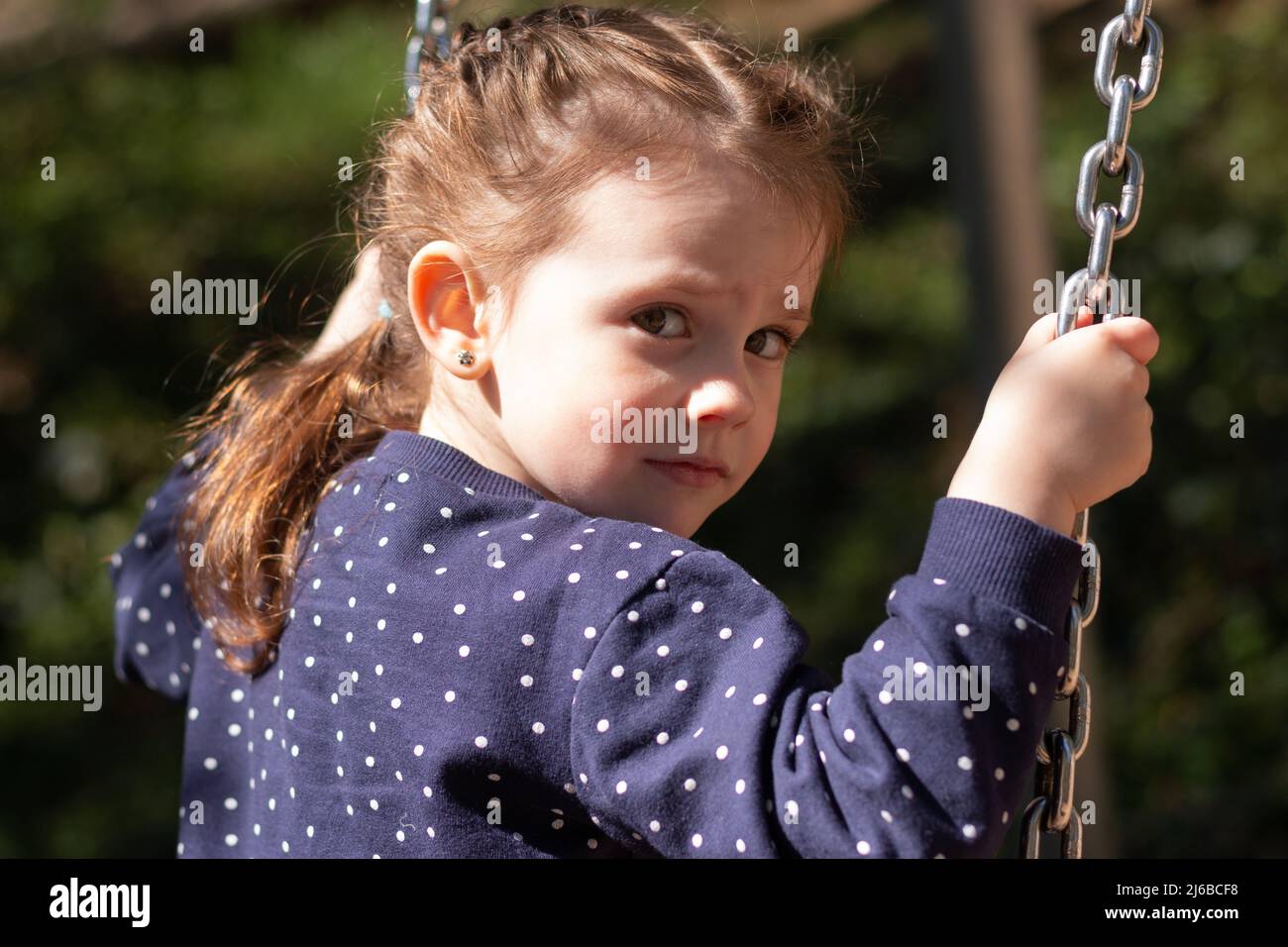 Little smiling girl turned around swinging on a swing outdoors on a ...