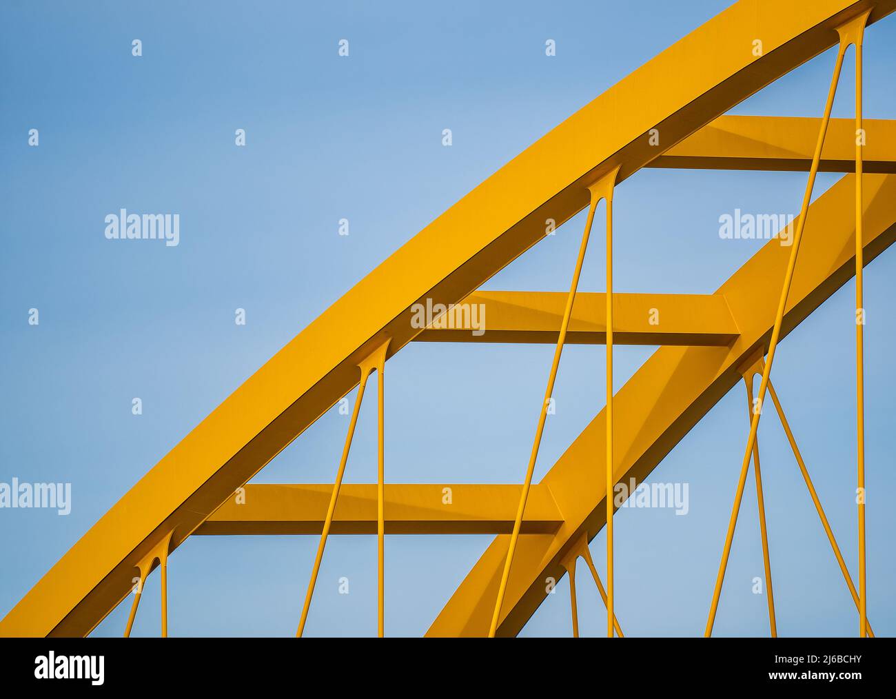 Yellow steel arch of a bridge against a steel blue sky. Visble are the ...
